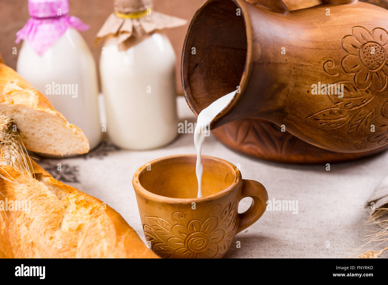 Pitcher of milk being poured into wooden cup surrounded by bottles ...