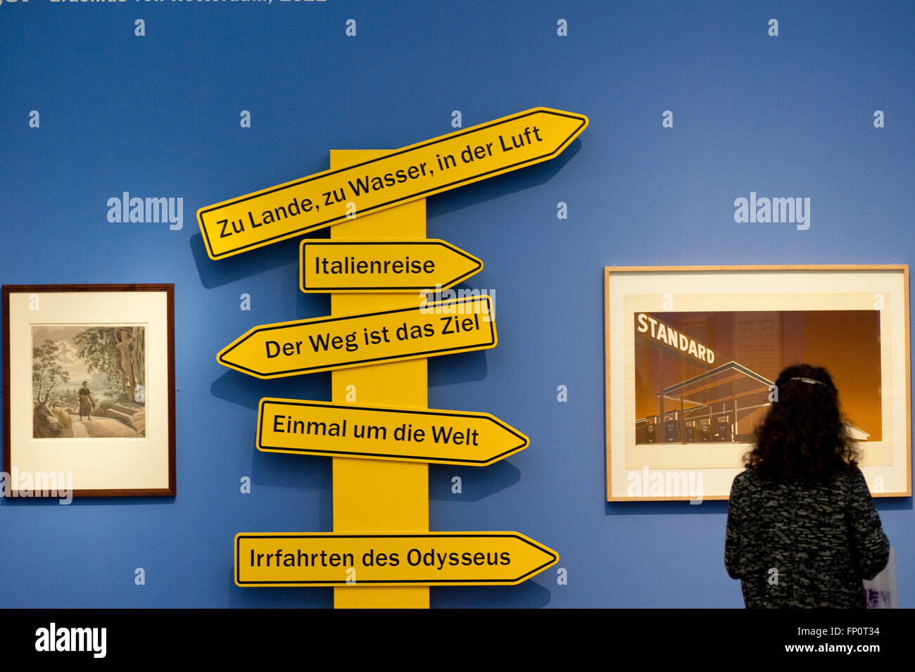 A woman standing in front of paintings and a signpost at the exhibition ...