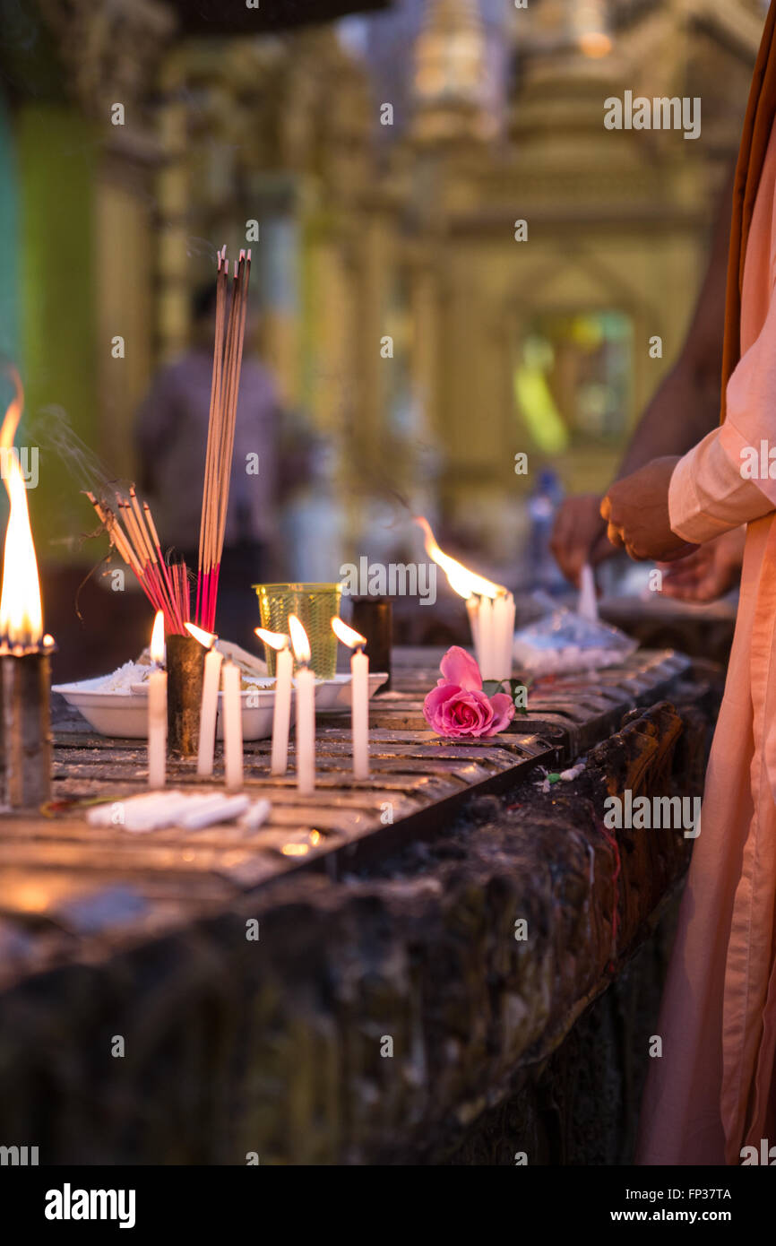 Myanmar, Yangon. Buddhist Monk places offering candles at an altar at ...