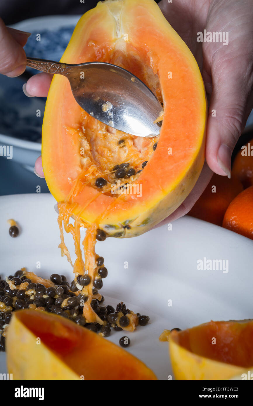 cleaning a papaya with a spoon up close dropping the seeds on a white ...
