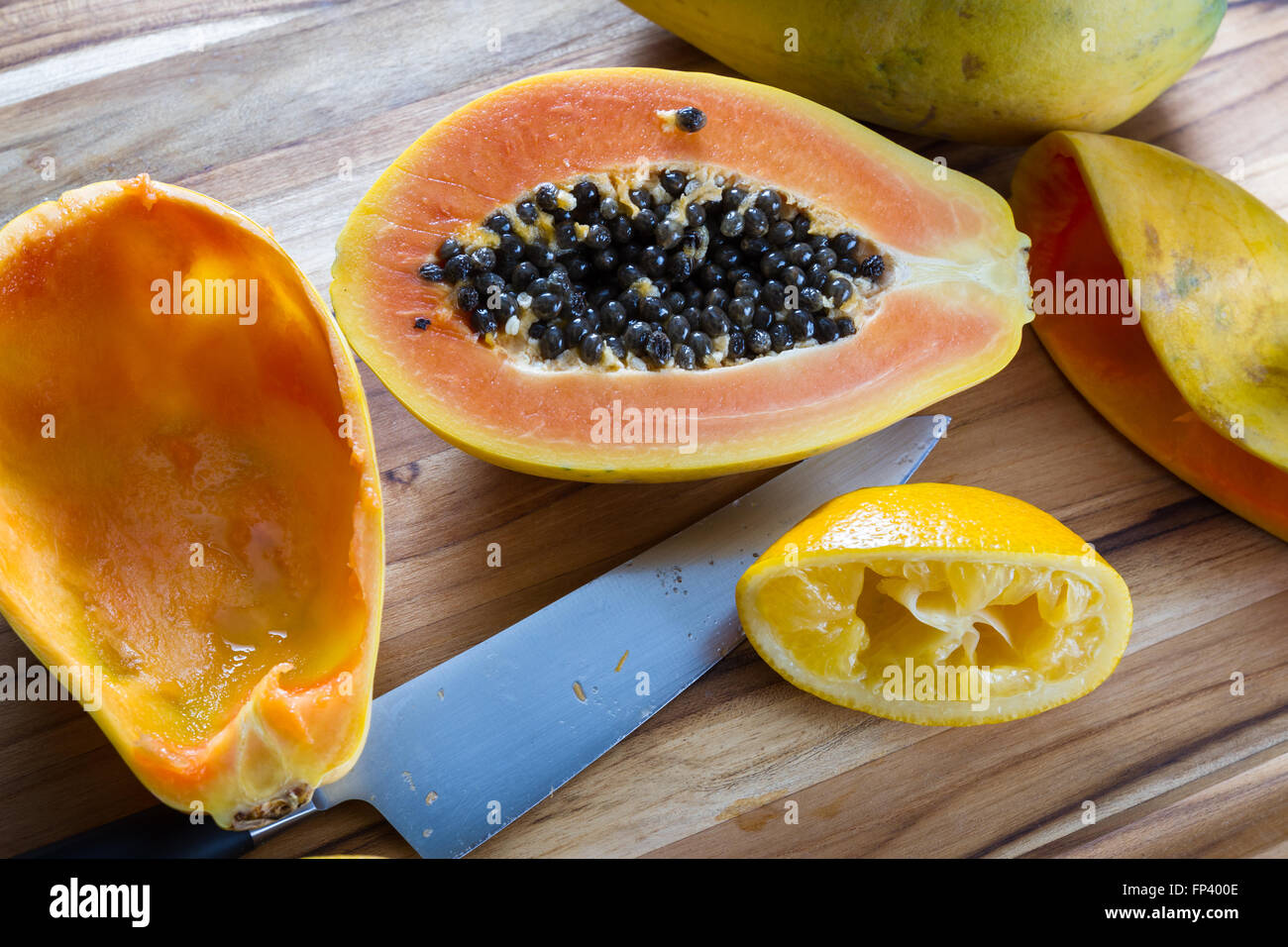 close up of a papaya cut in half on a wooden cutting board served with ...