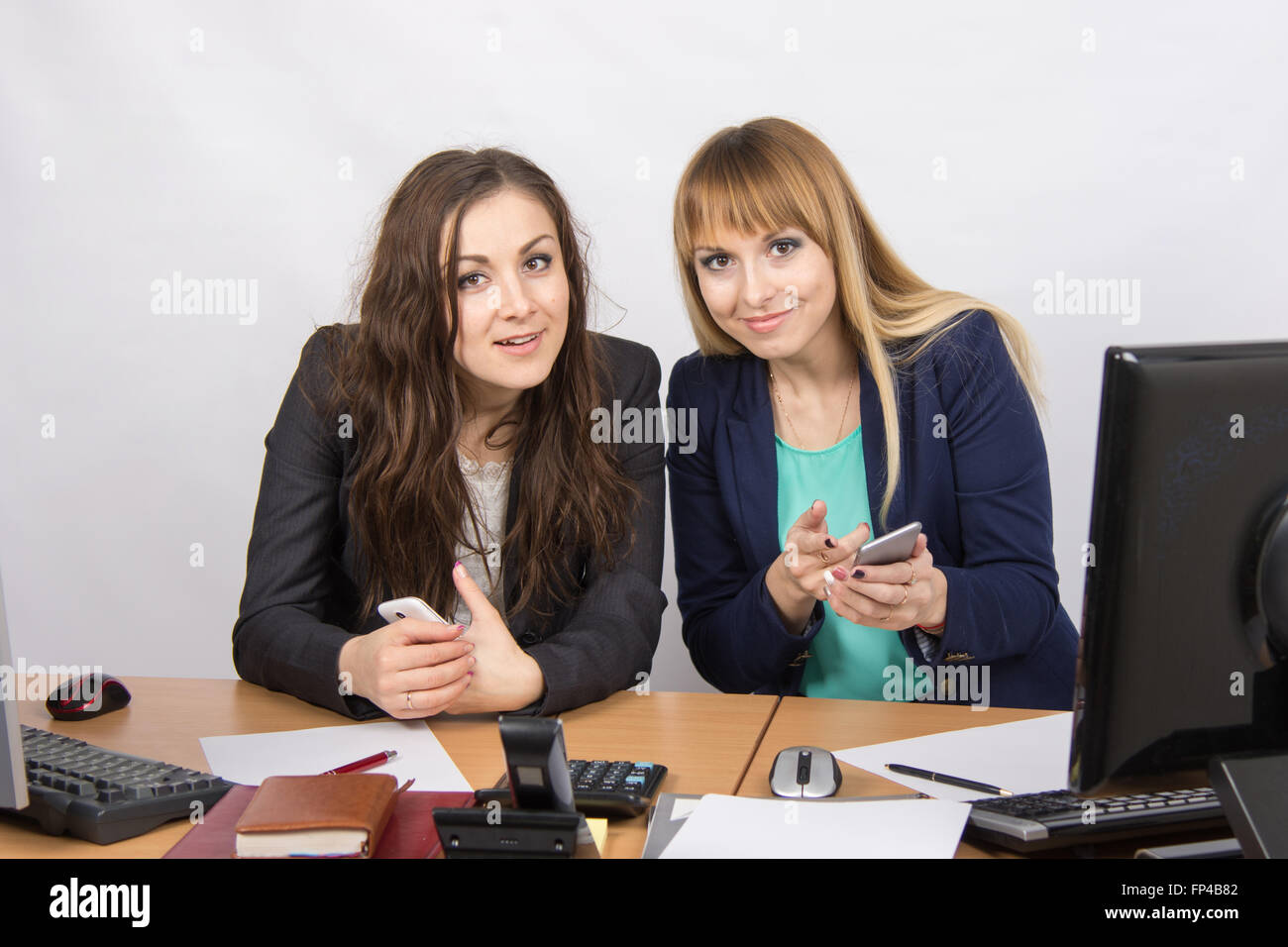 Two young office employee engaged in personal business in mobile phones ...