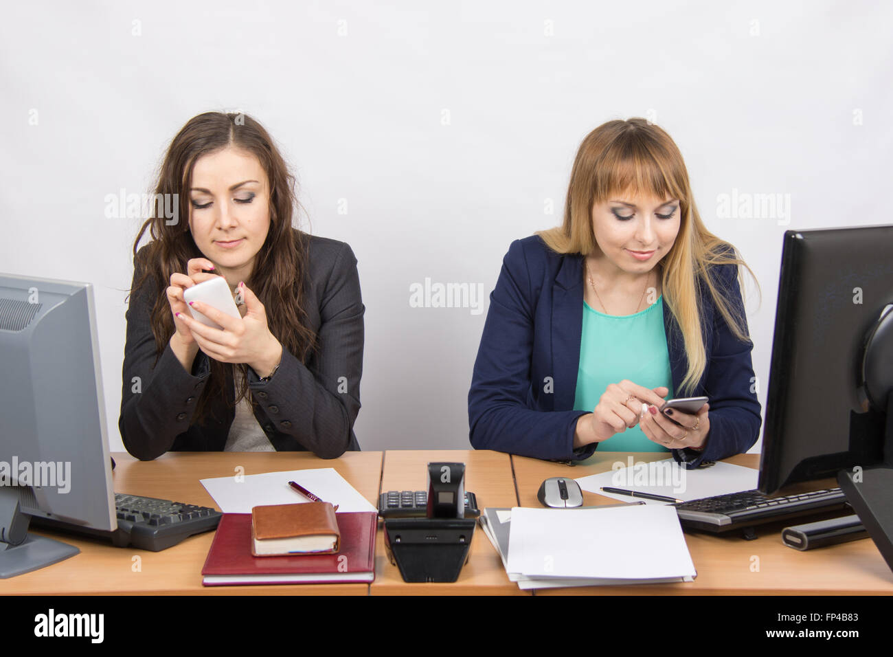 Two young office employee engaged in personal business in mobile phones ...
