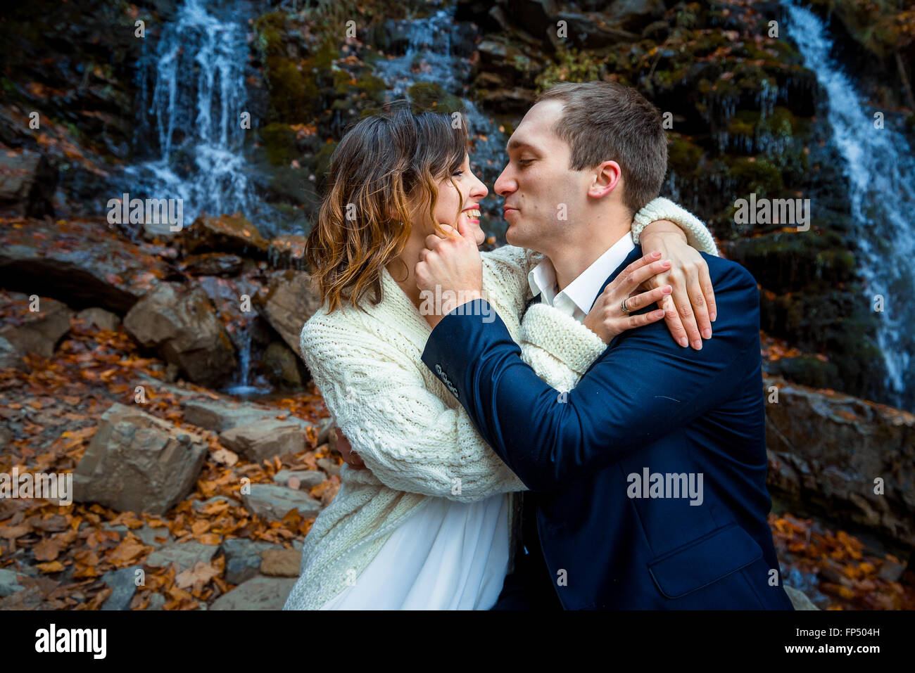 Handsome groom softly touches face of his bride. Waterfall on ...