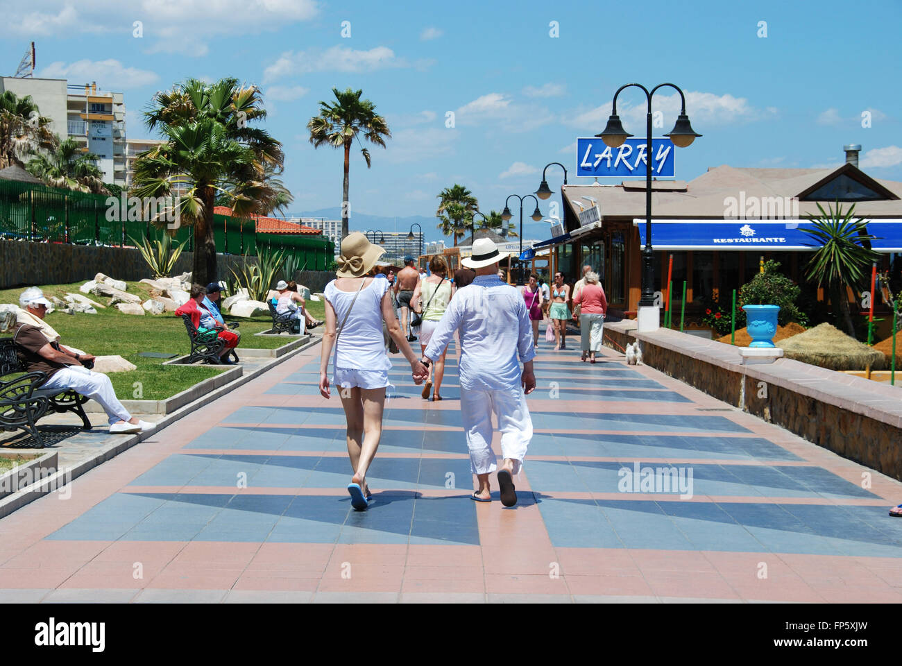 Tourists walking along the promenade with beach bars to the right hand ...