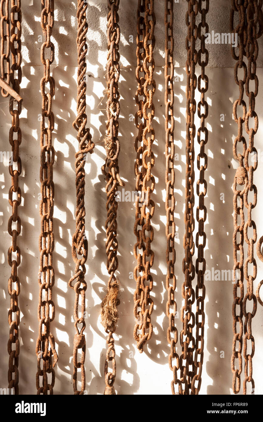 Rusty chains hanging on sunlit barn wall Stock Photo - Alamy