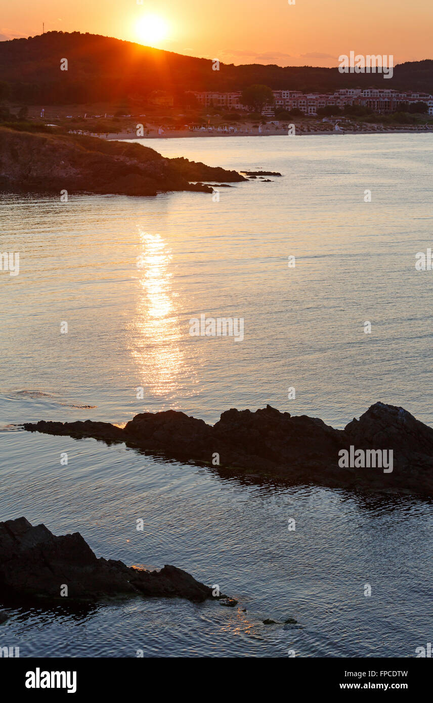 Sunset sea rocky coast view with sun track on water surface and town ...
