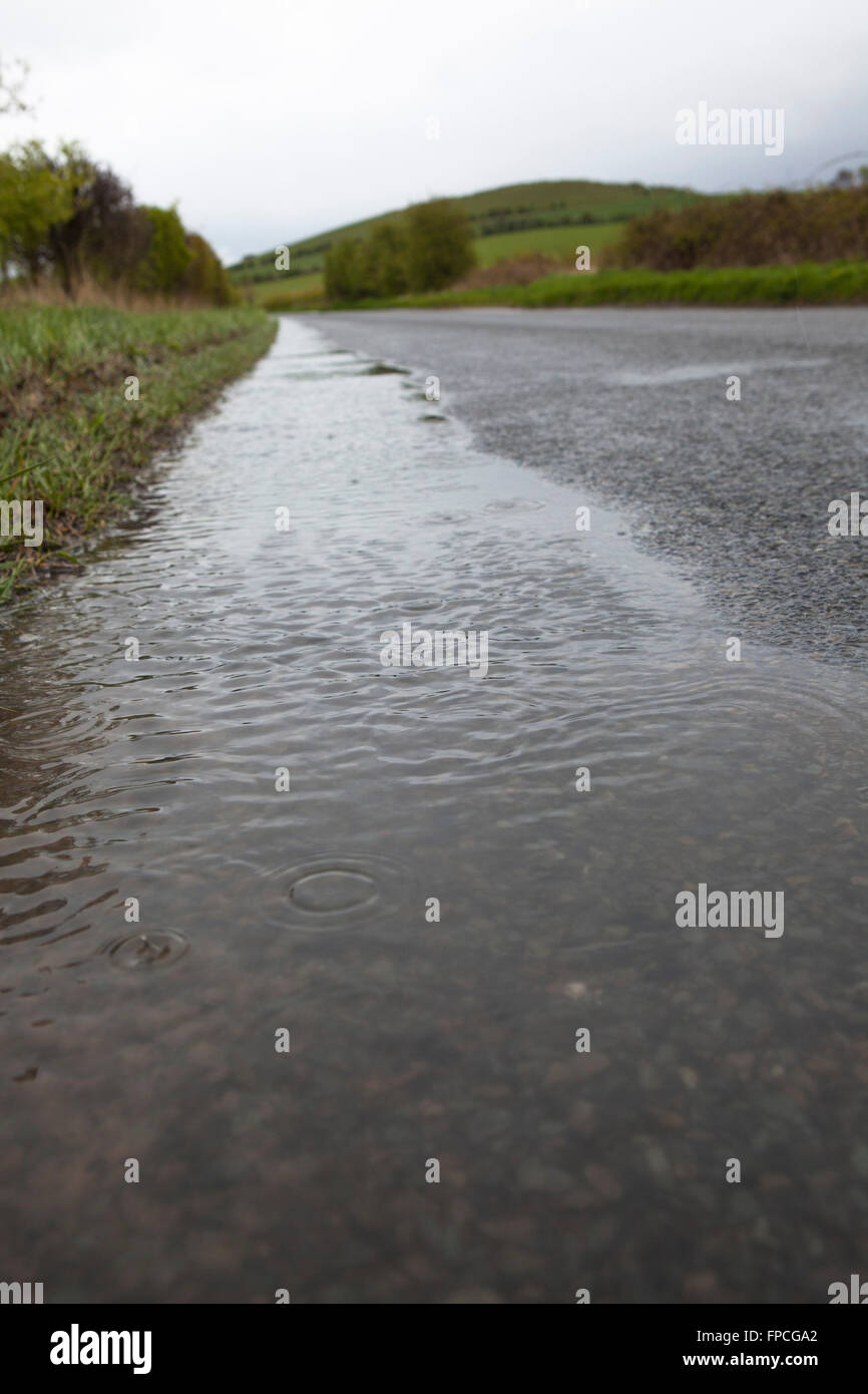 Rainwater runs down the gully or roadside of a country lane after a ...