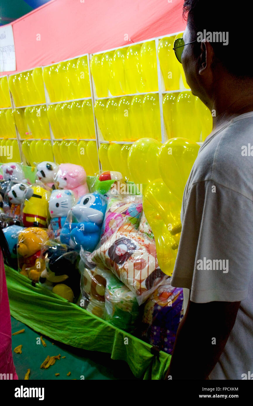 A man is looking at an arcade game where people throw darts at balloons ...
