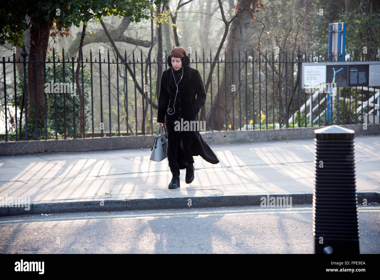 Woman in black crossing road ear muffs headphones Stock Photo - Alamy