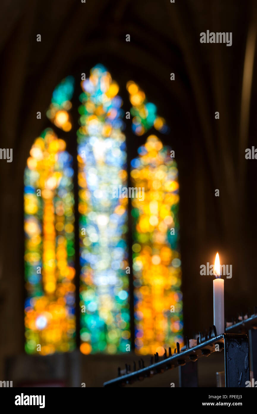 Single lit prayer candle in front of a modern stained glass window in ...