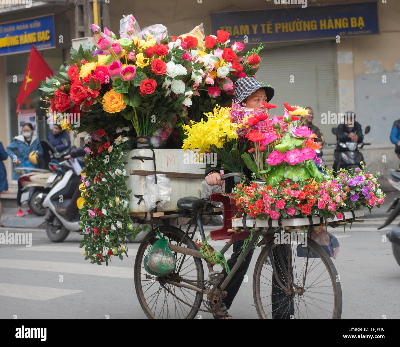 HANOI, VIETNAM - JANUARY 21, 2016: A flower seller taking her mass of flowers on her bicycle to ...