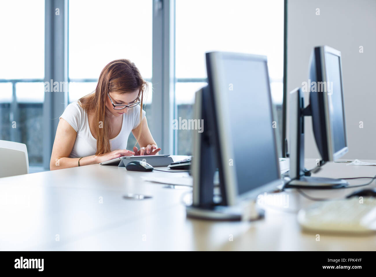 Pretty, female student looking at a desktop computer screen, learning ...