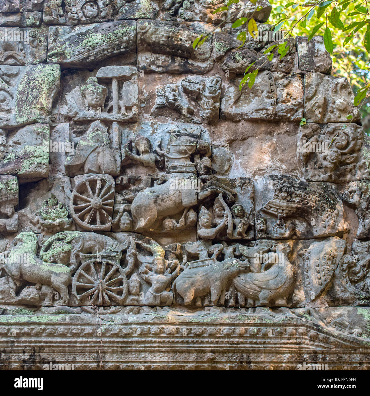 Lichen covered broken bas relief in a wall showing carts, soldiers ...