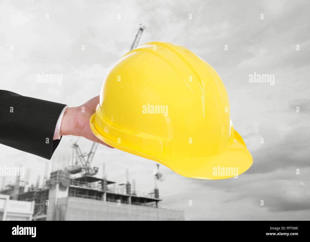 hand of engineer holding yellow helmet with construction crane ...