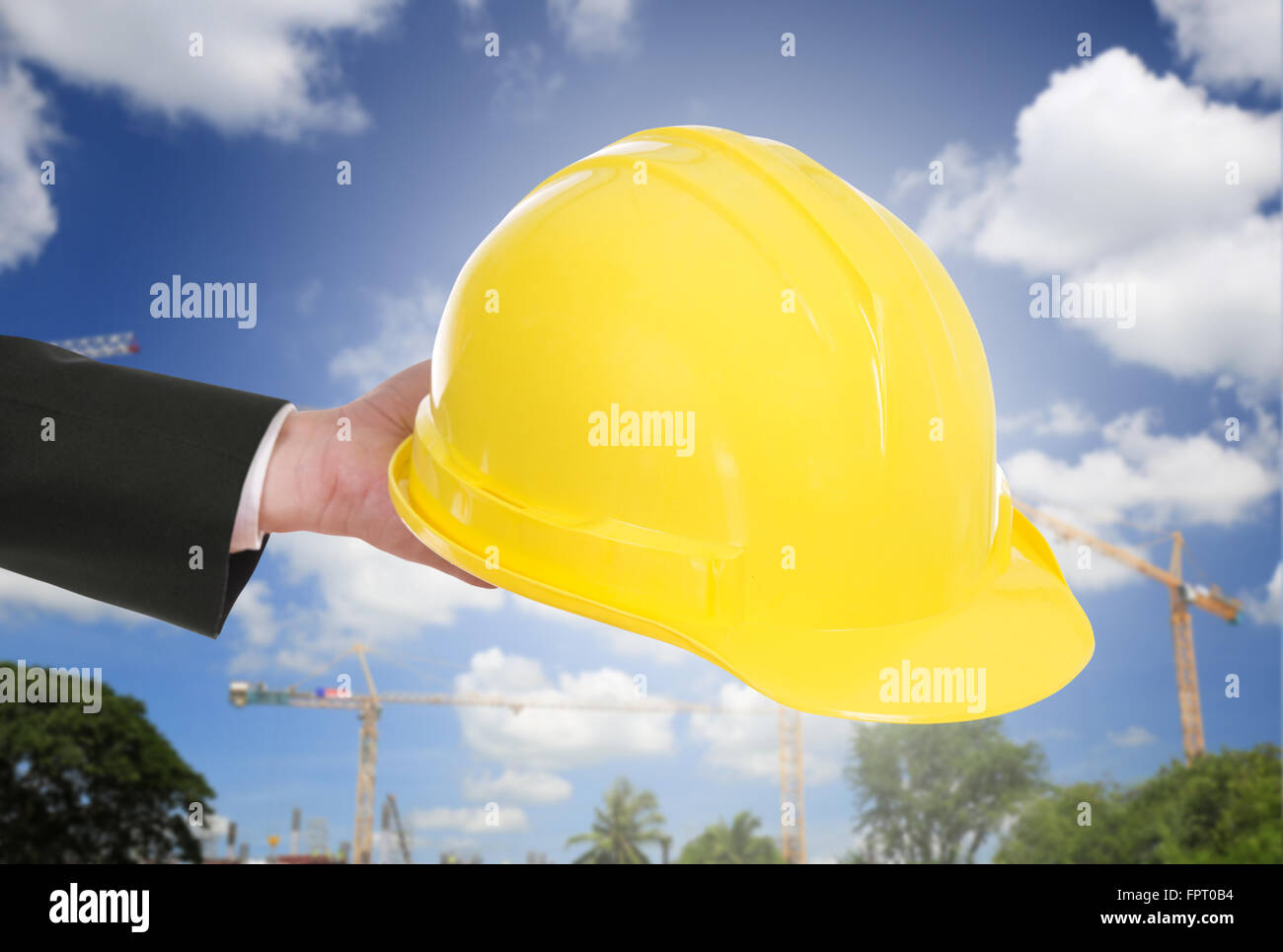 hand of engineer holding yellow helmet with construction crane ...