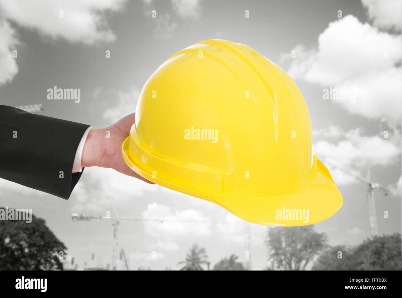 hand of engineer holding yellow helmet with construction crane ...