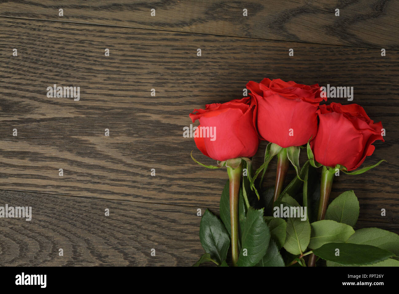 three red roses on wood table Stock Photo - Alamy