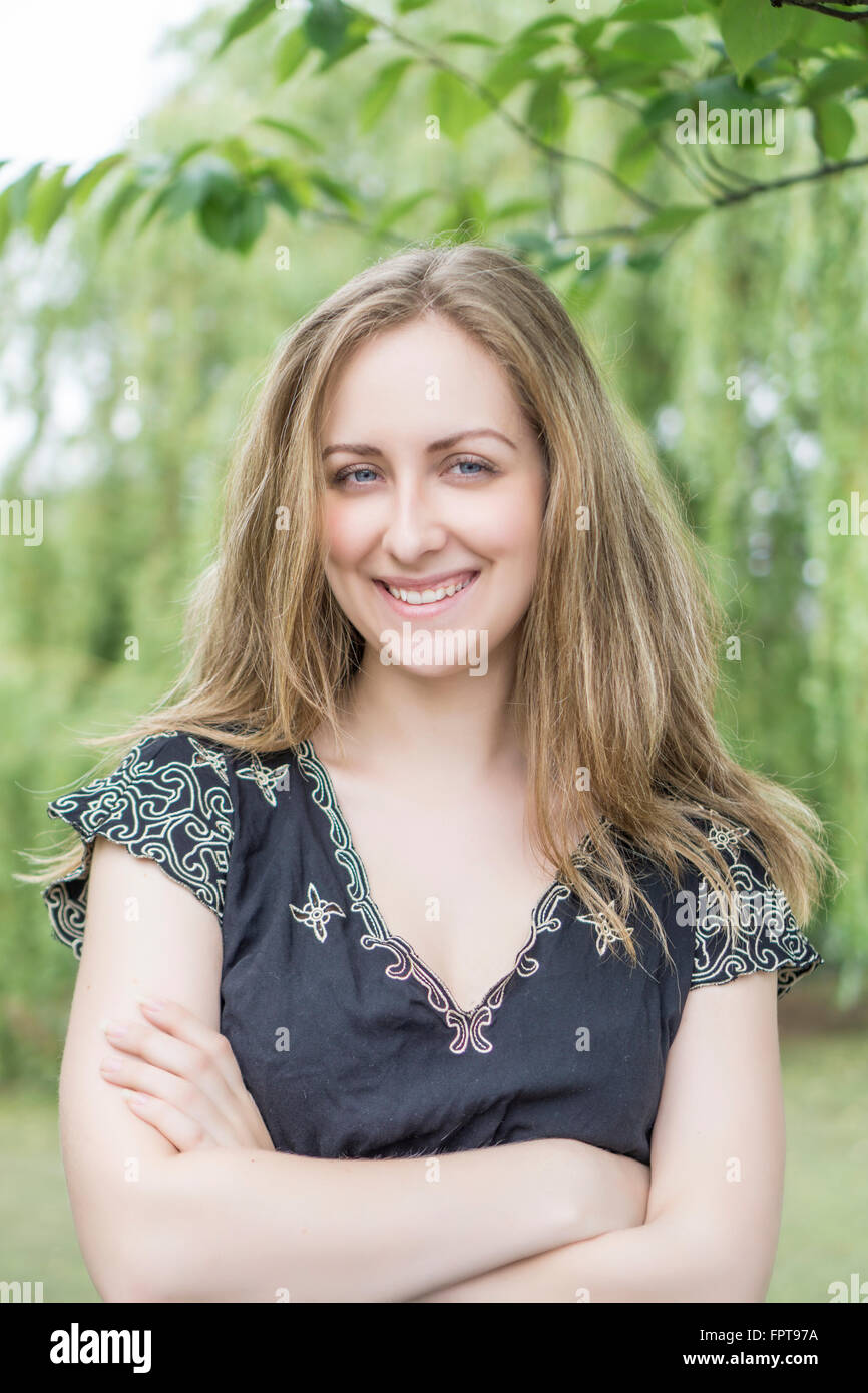 Attractive young woman arms folded smiling outdoors Stock Photo - Alamy