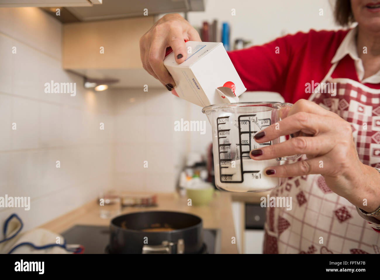 Senior woman filling icing sugar into a measuring cup in kitchen ...