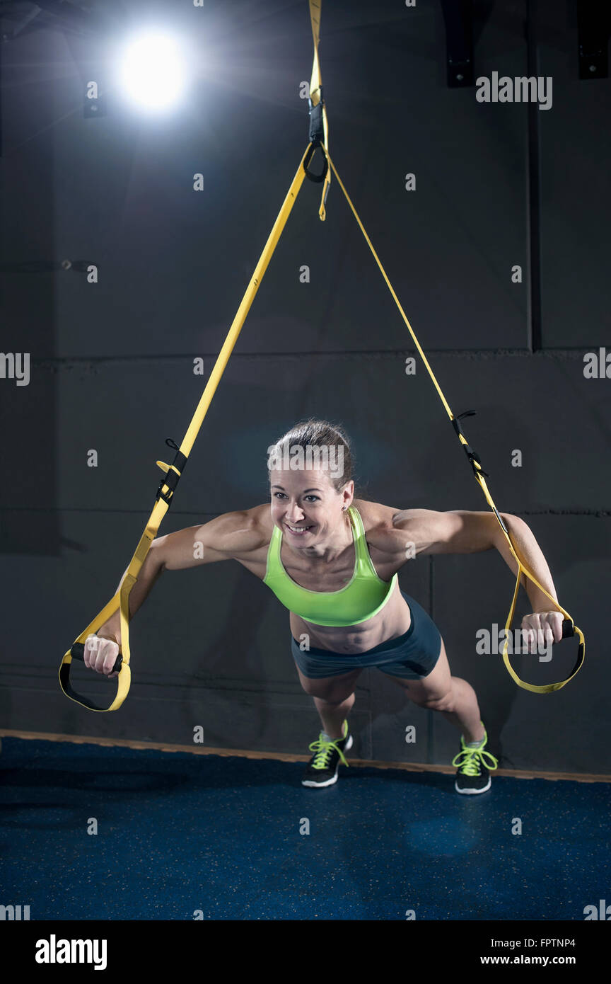 Sportive woman doing press-ups with TRX belt in health club, Bavaria ...
