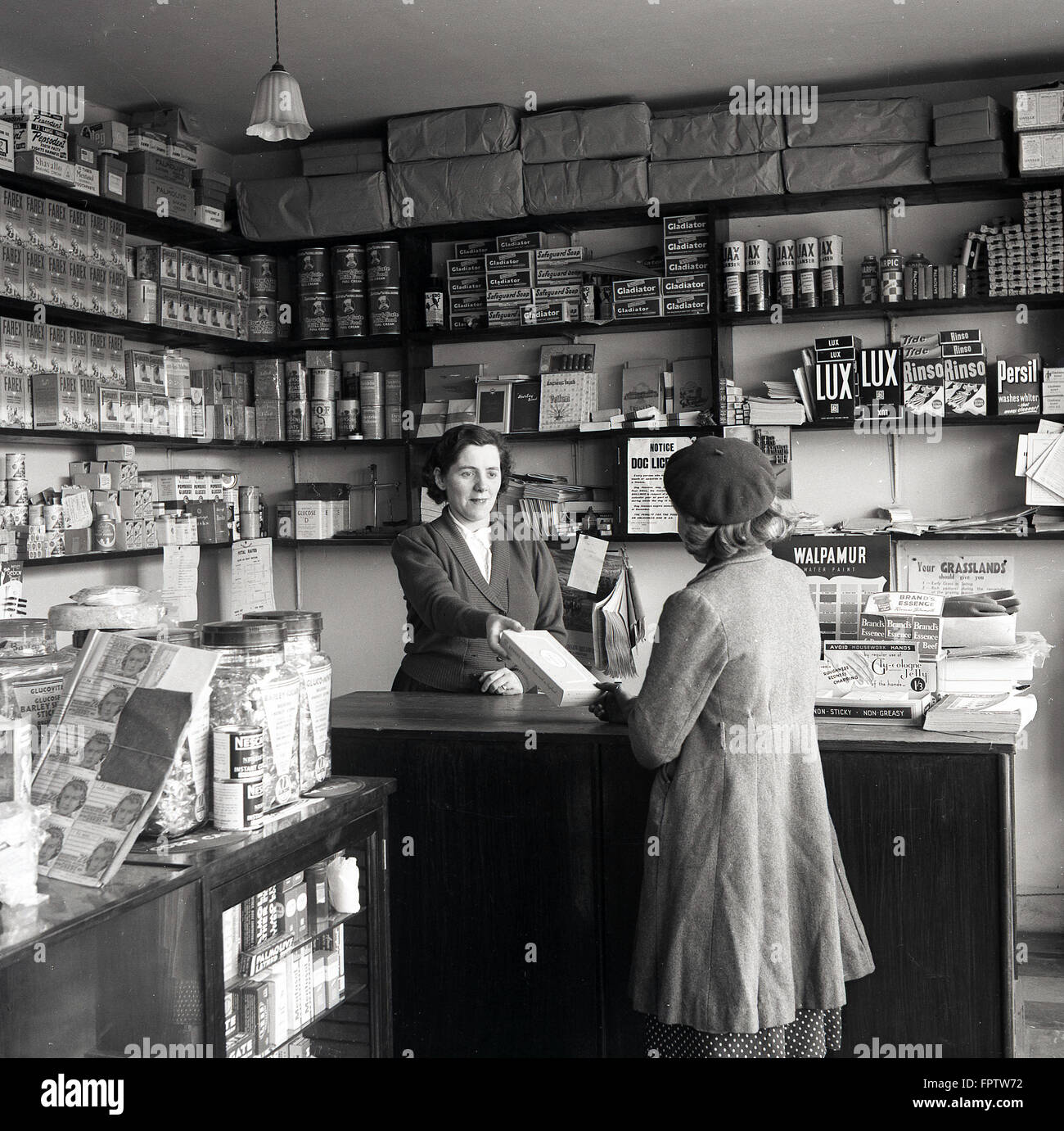 1950s historical, female assistant serving lady customer with child in ...