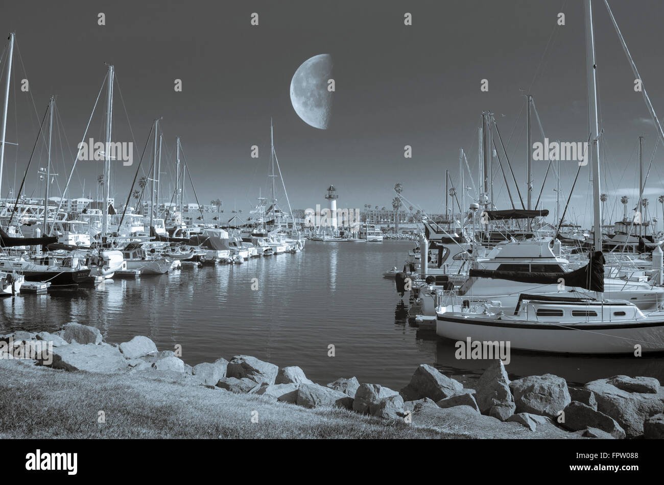 Black and white image of harbor with boats docked and large moon over ...