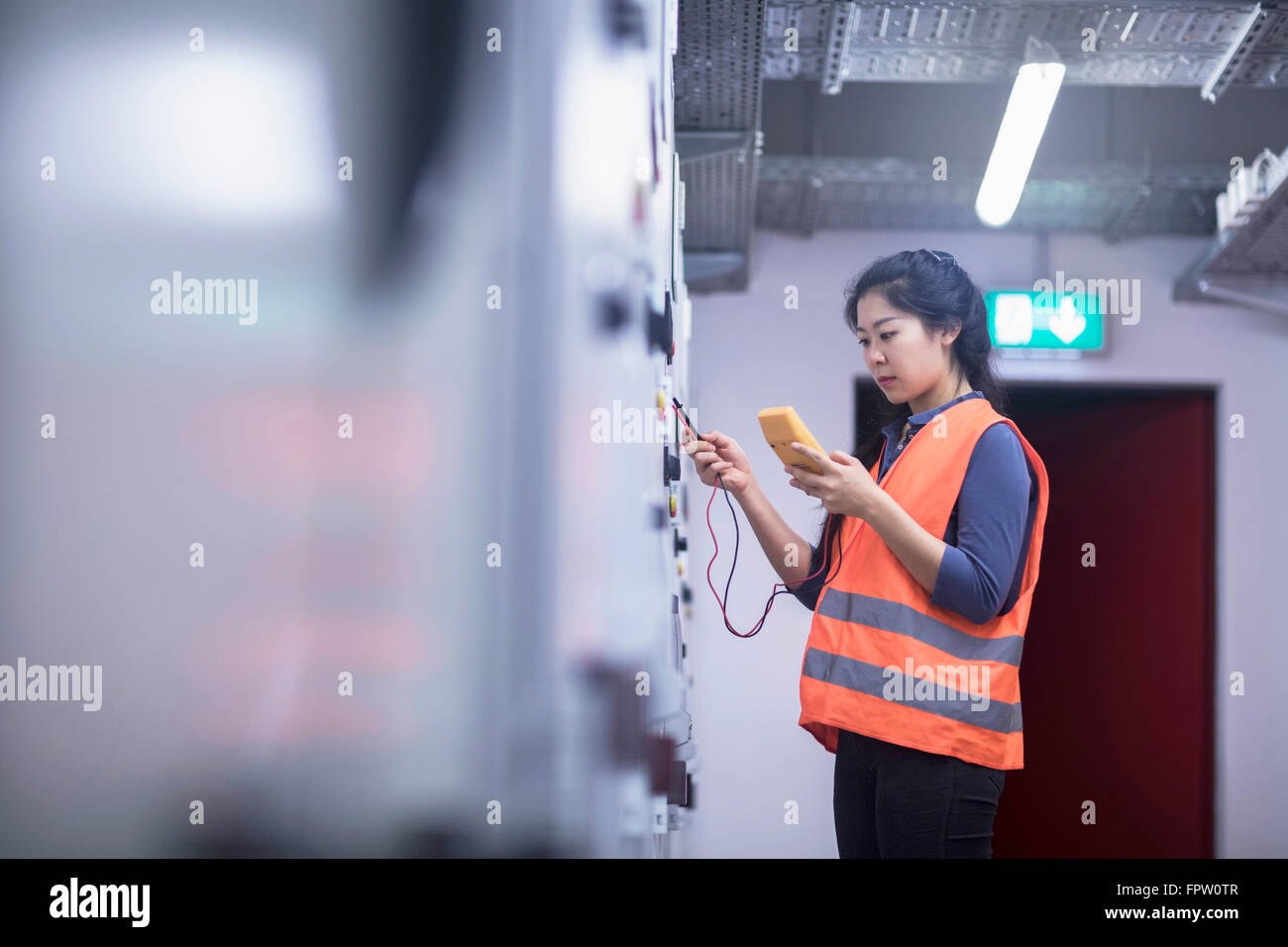 Young female engineer examining control panel with multimeter in an ...