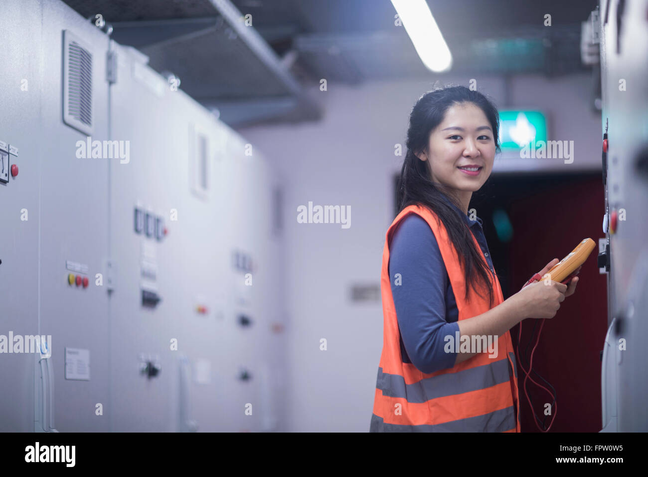 Young female engineer examining control panel with multimeter in an ...
