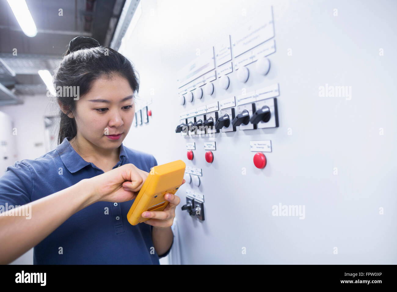 Young female engineer examining control panel with multimeter in an ...