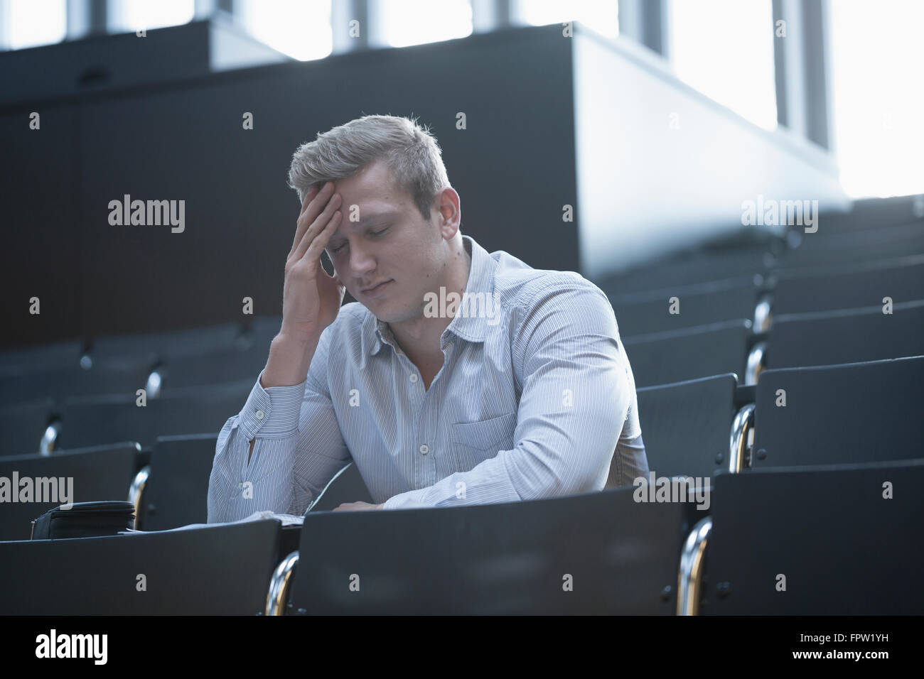 Young man sitting with tension in lecture hall with head in hands ...