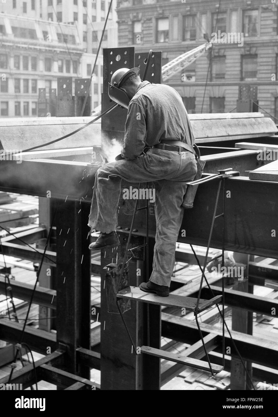 1950s SIDE VIEW OF CONSTRUCTION WORKER WELDING ON STEEL GIRDER FRAME OF ...