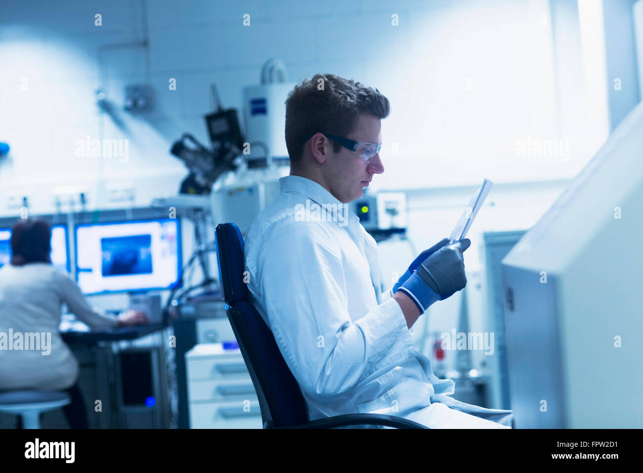 Young male scientist looking at report in an optical laboratory ...