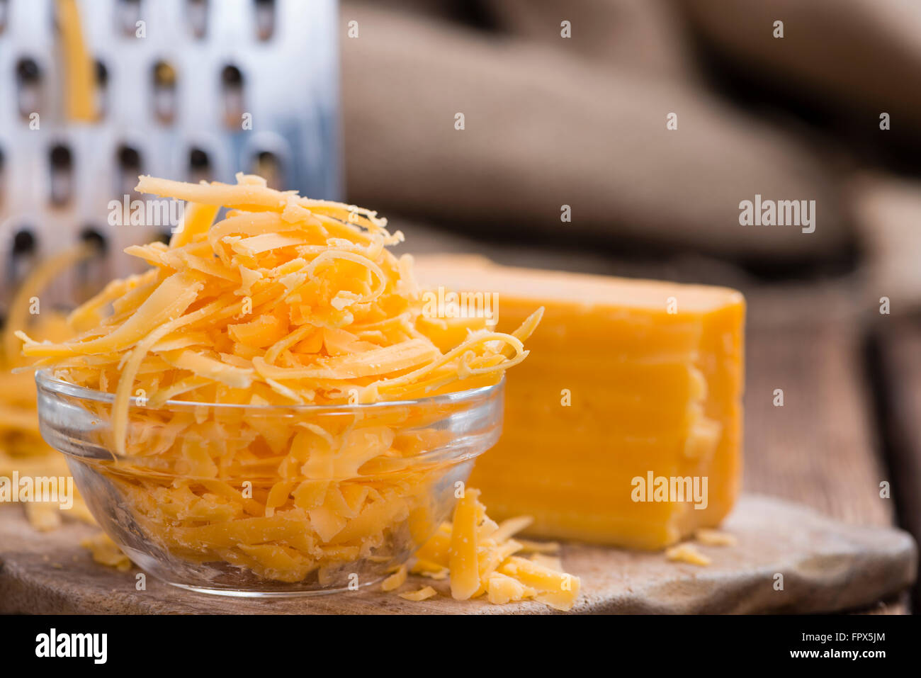 Grated Cheddar Cheese in a small bowl on rustic wooden background Stock ...