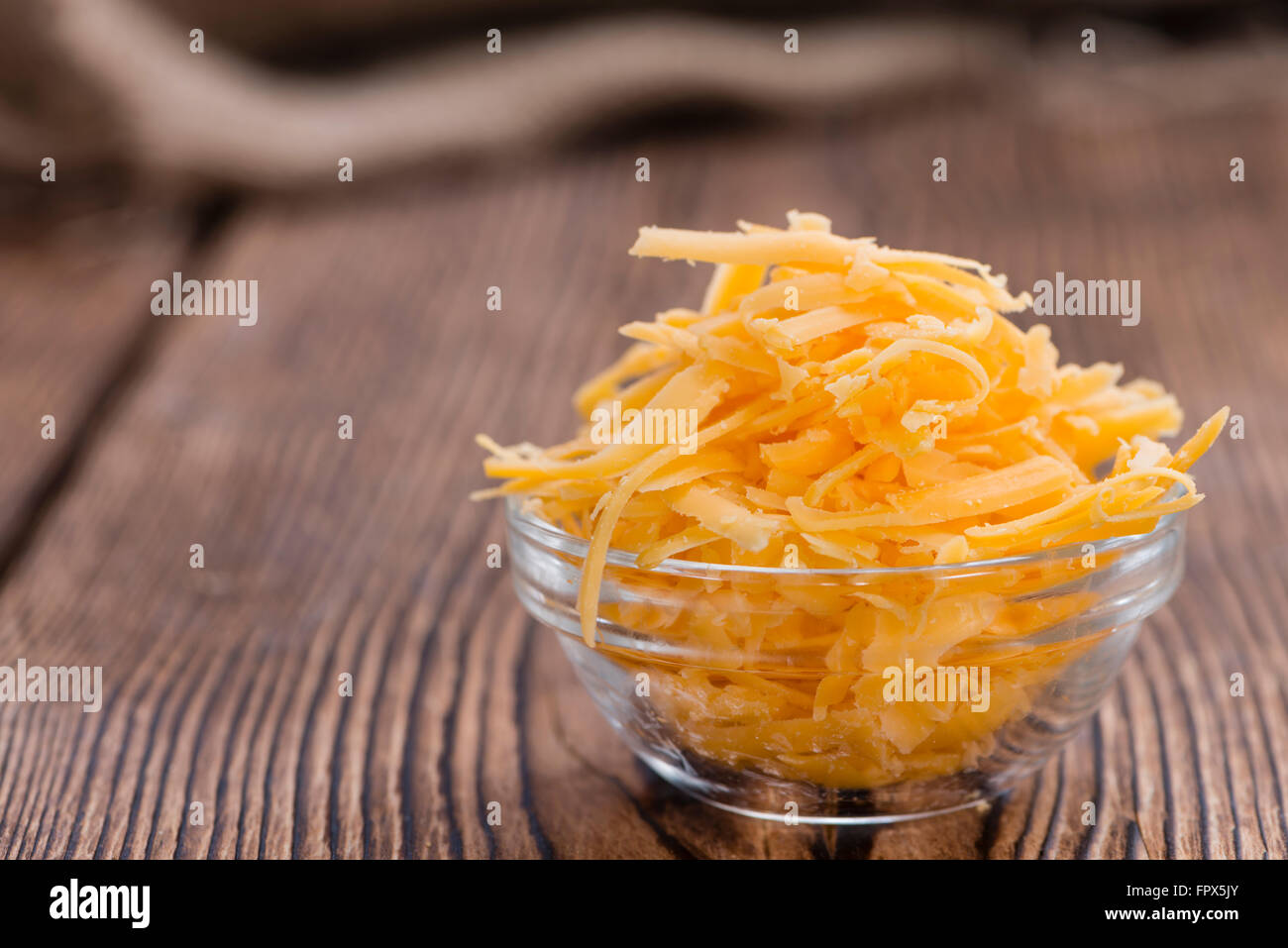 Heap of grated Cheddar Cheese (close-up shot) in rustic background ...