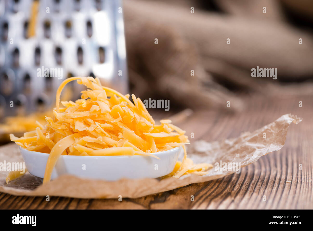 Heap of grated Cheddar Cheese (close-up shot) in rustic background ...