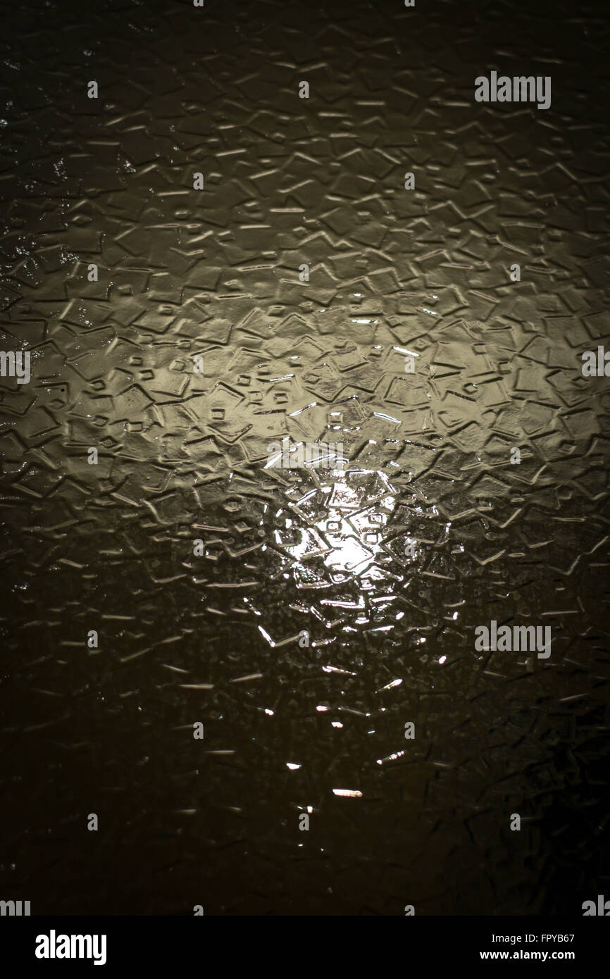 Home interior lightbulb shines through a dark glass window creating ...