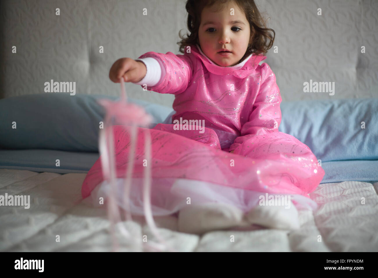 Little girl costumed as a fairy with magic wand sitting on the bed and ...