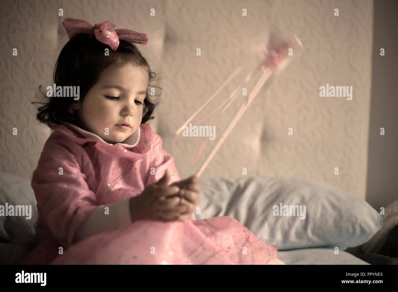 Little girl costumed as a fairy with magic wand sitting on the bed and ...