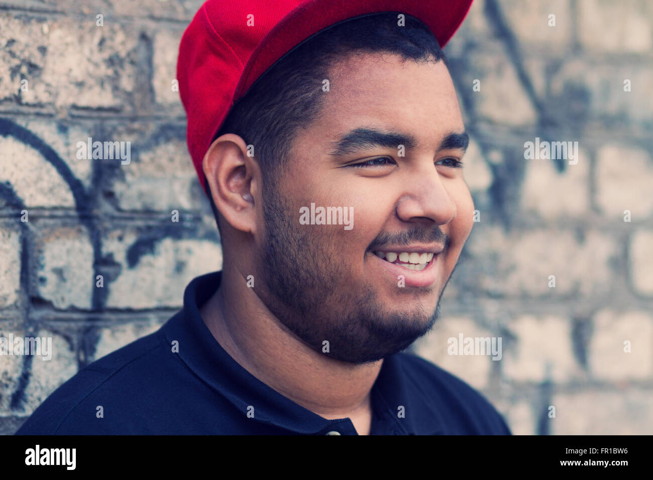 Happy black male in red cap posing outdoors on a grey brick wall ...