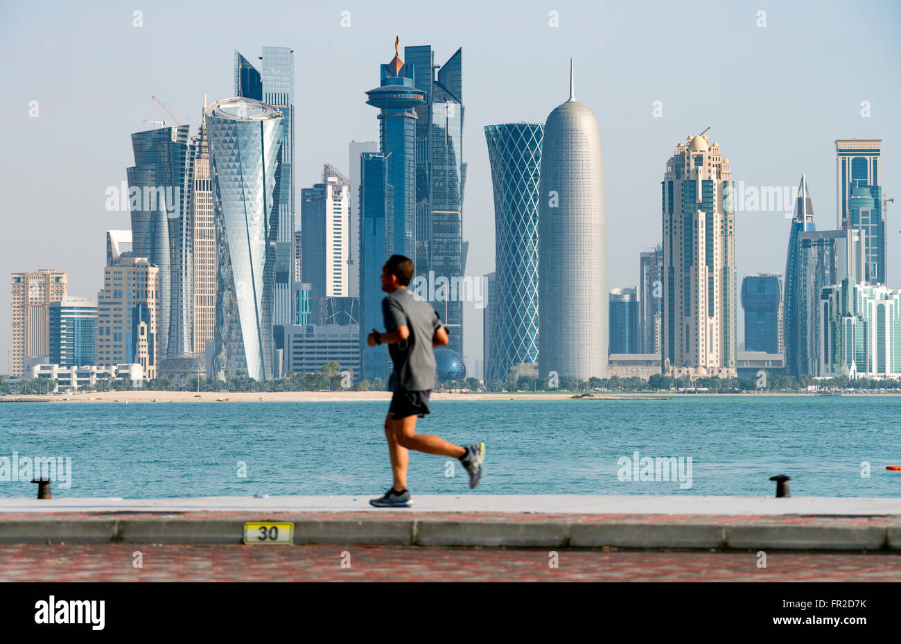 Mann jogging on waterfront of Corniche towards modern office towers in ...