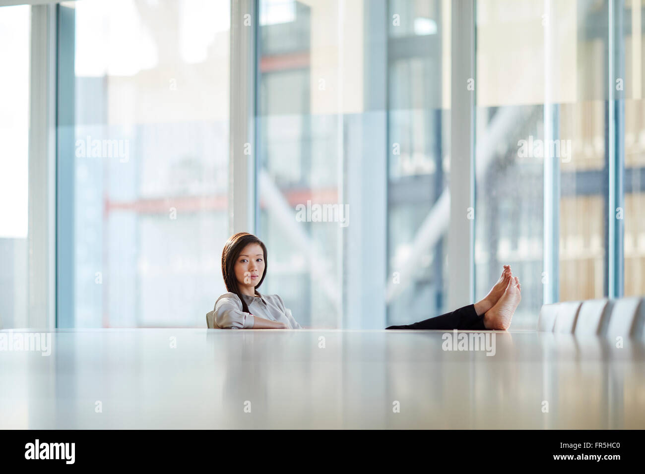 Portrait confident businesswoman with bare feet up on conference room ...