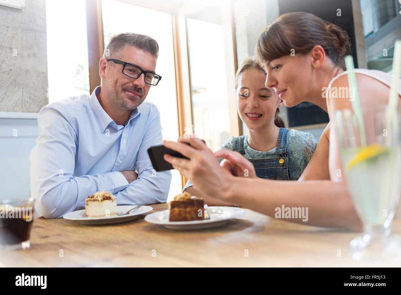 Family with cell phone eating dessert at cafe table Stock Photo - Alamy