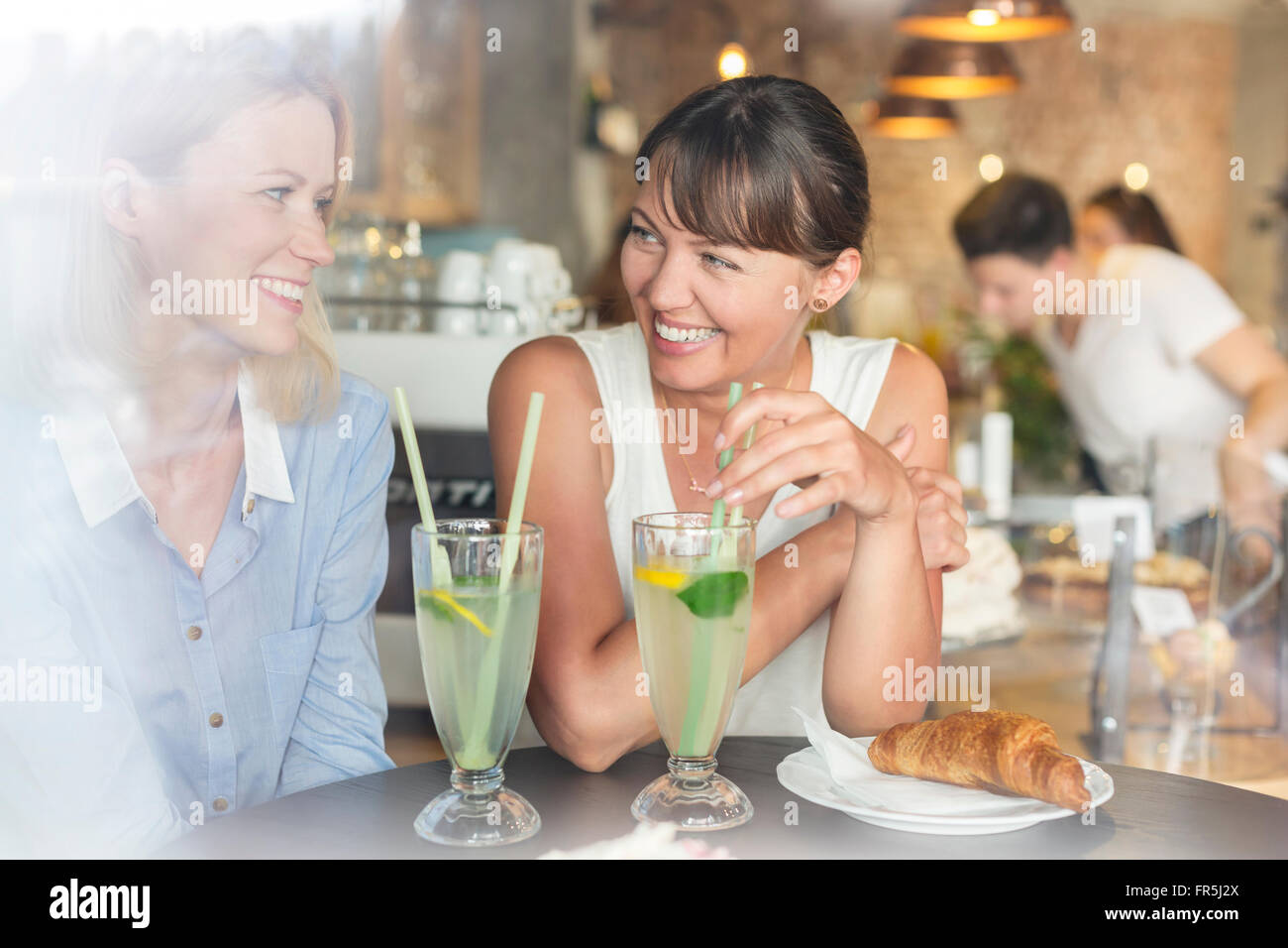 Smiling women drinking lemonade at cafe table Stock Photo - Alamy