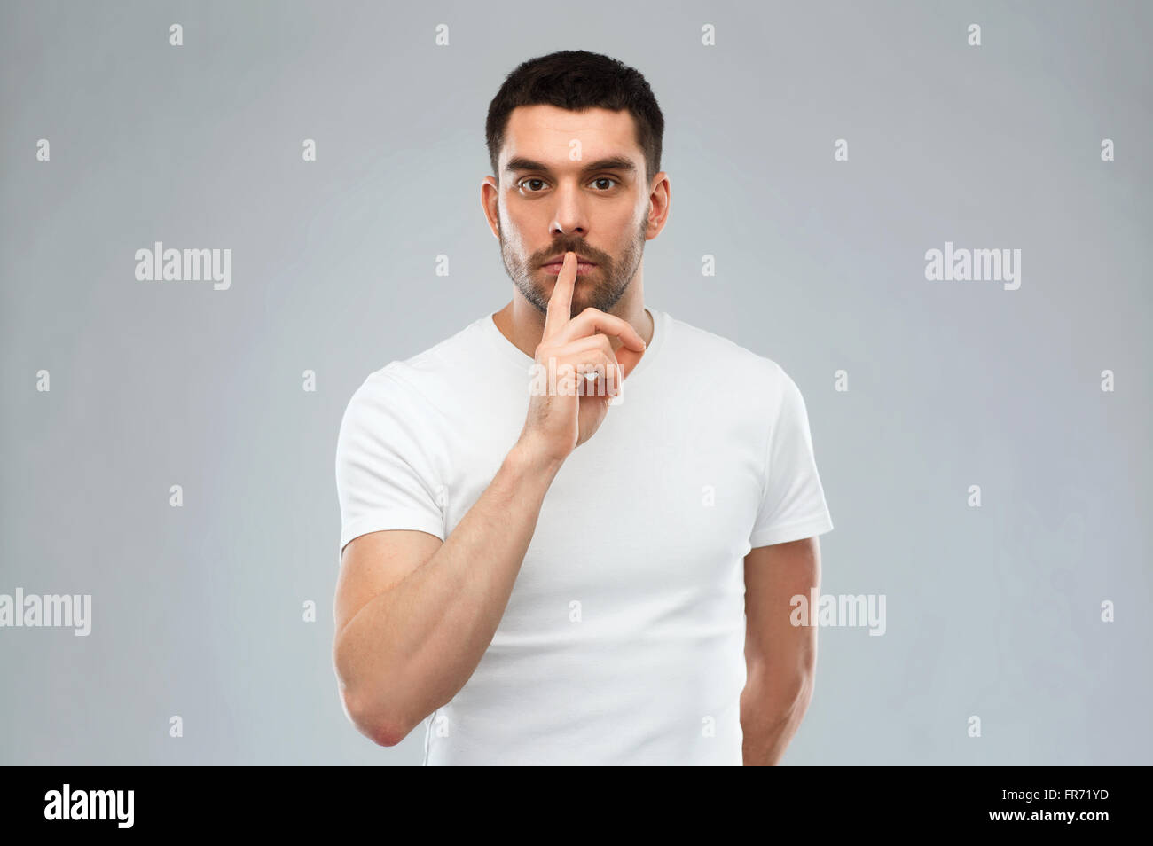 young man making hush sign over gray background Stock Photo - Alamy