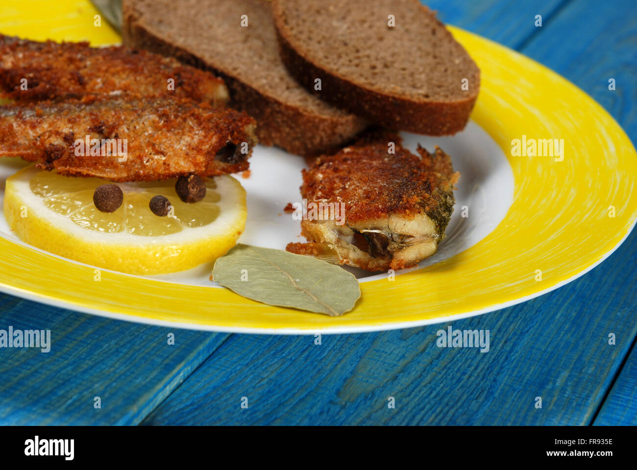 Grilled fish with lemon, bread, round pepper and bay leaf on a plate on ...