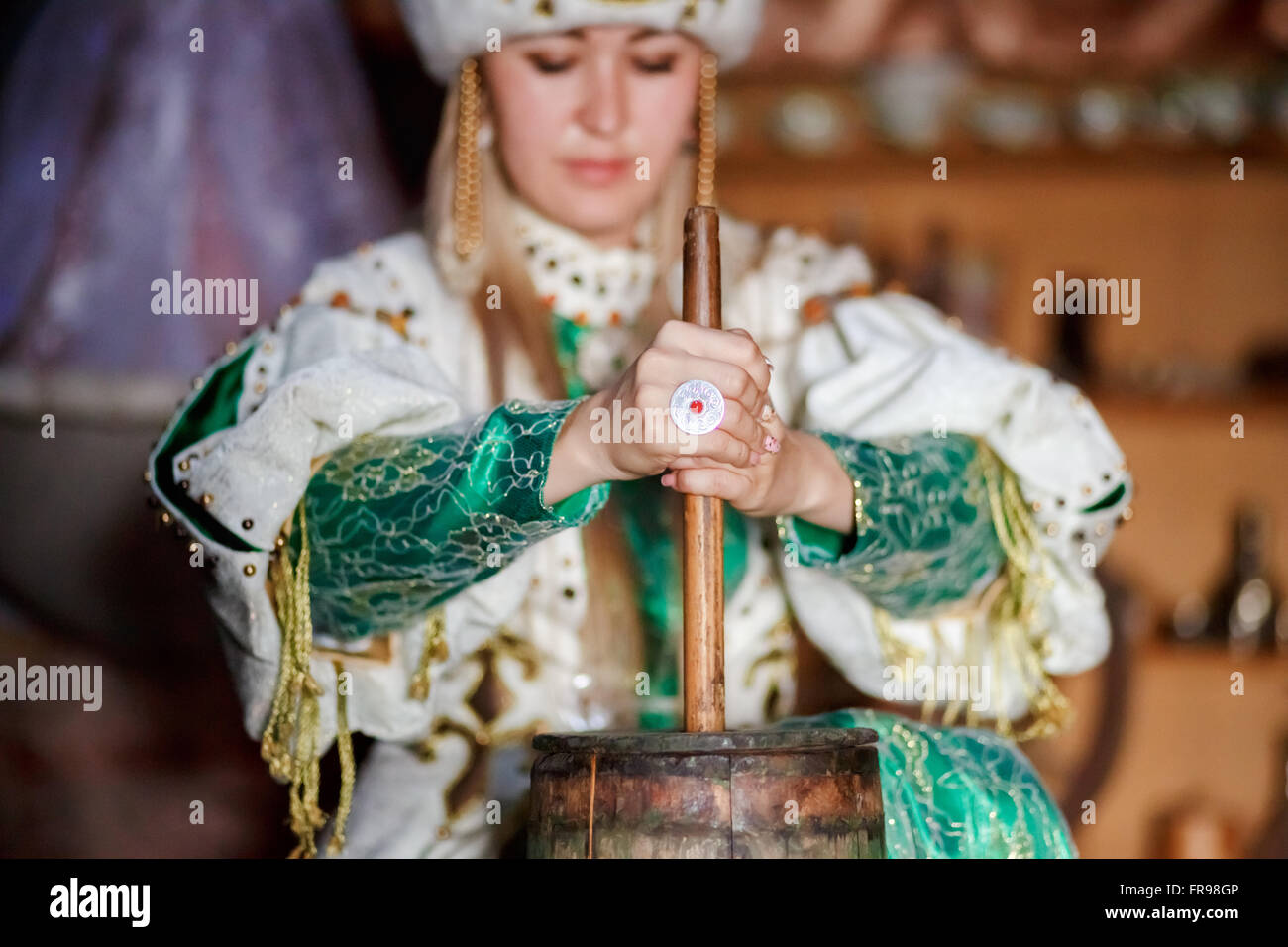Young woman in traditional dress producing butter from milk at home ...