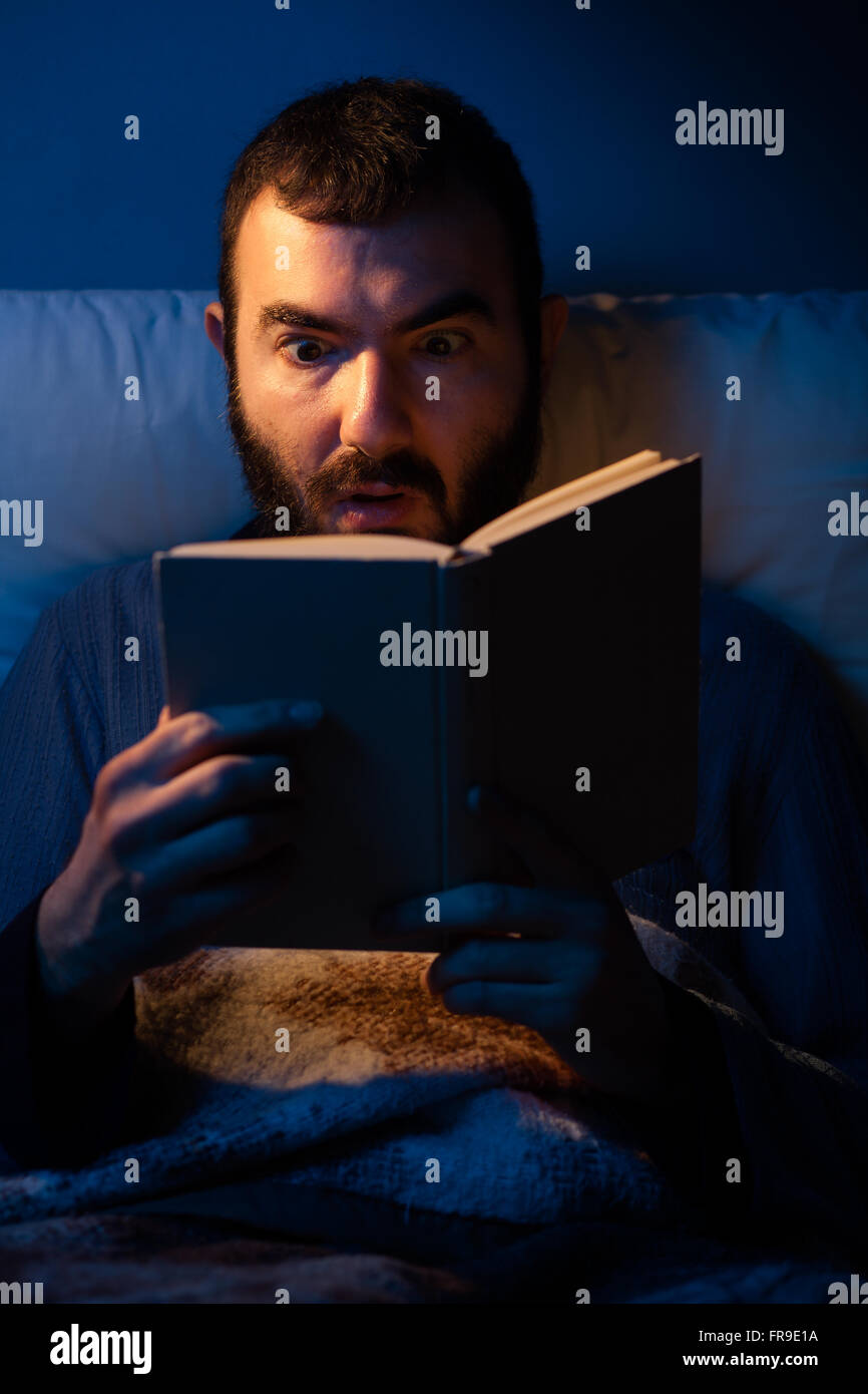 Surprised Man Reading a Book at Night in a Bed Stock Photo - Alamy