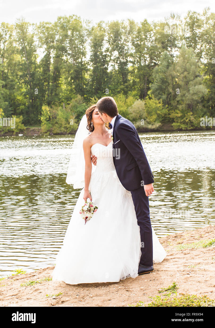 Wedding couple standing and kissing near lake Stock Photo - Alamy