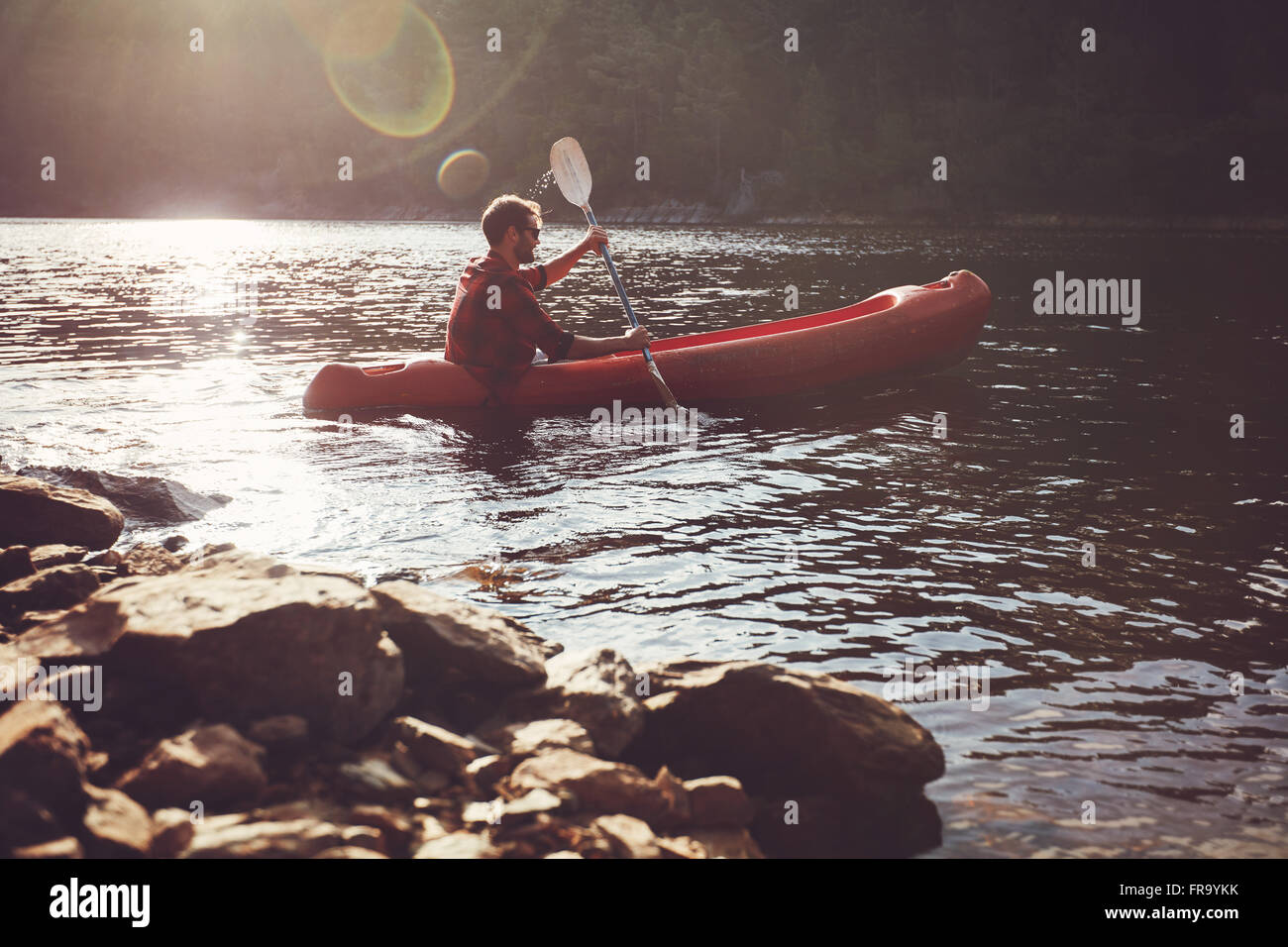 Young man kayaking in a lake. Young guy paddles his kayak on a sunny ...